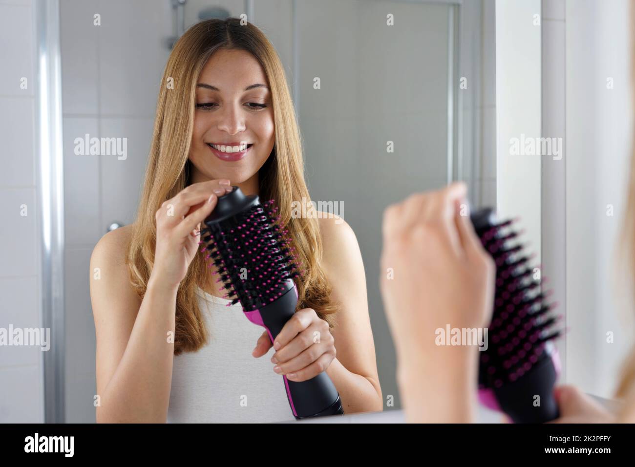 Pleased girl holds round brush hair dryer in her bathroom at home ...