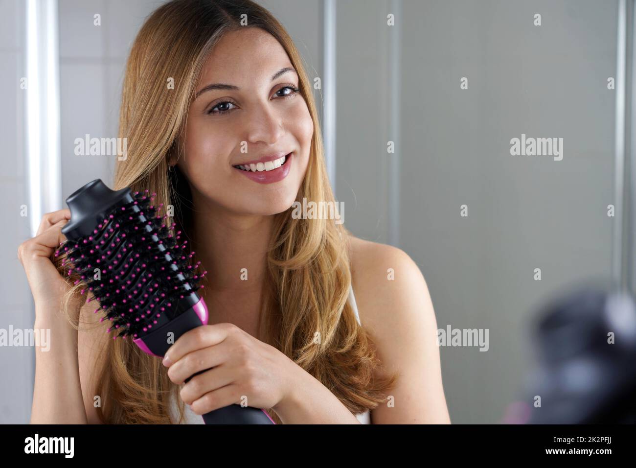 Pleased Girl Holds Round Brush Hair Dryer To Style Hair In Her Bathroom At Home Young Woman