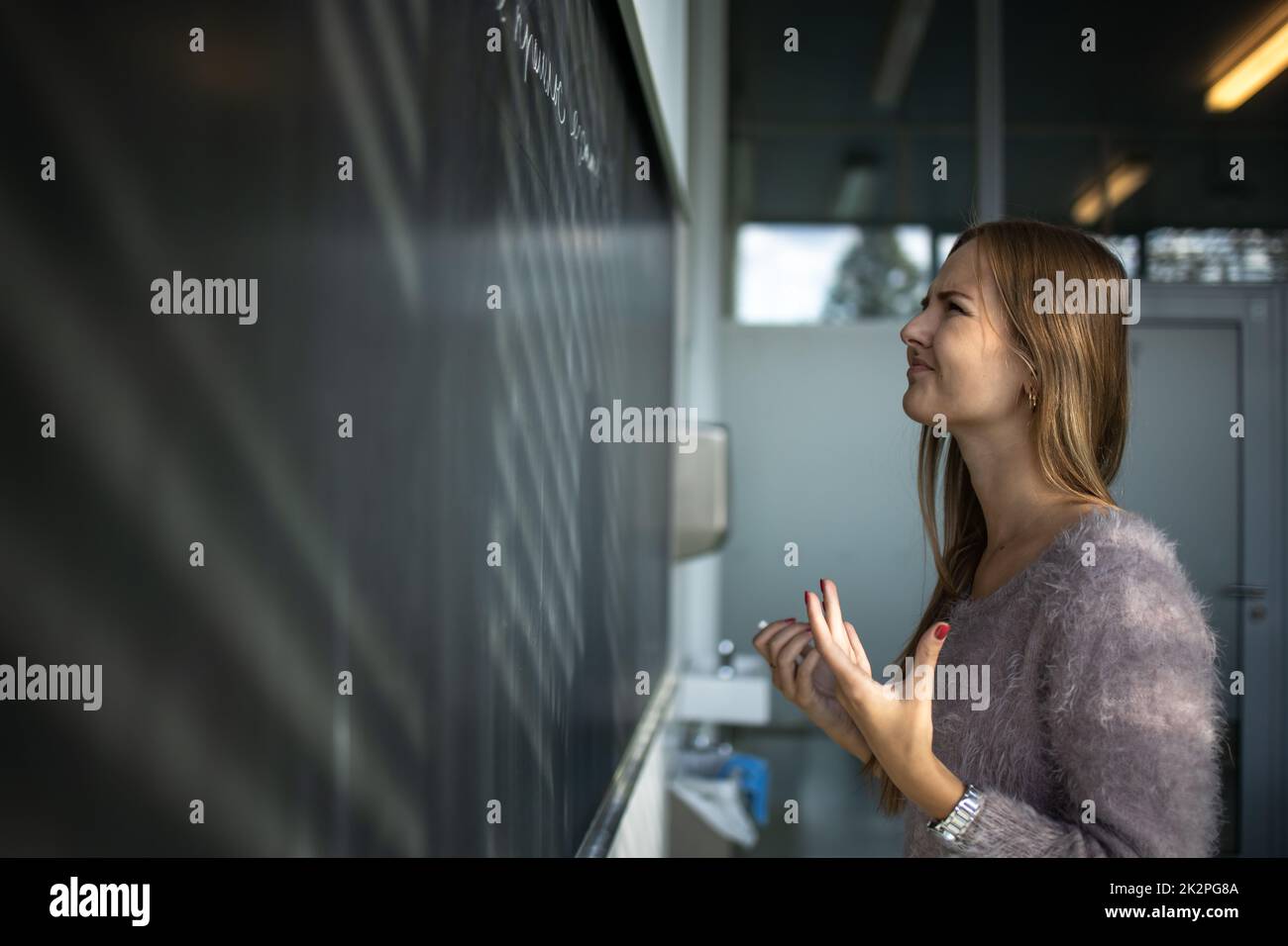 Pretty, young female student in front of a blackboard during math class ...