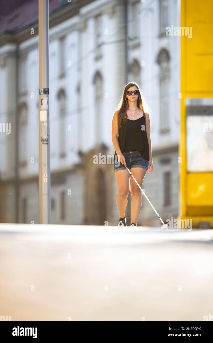 Blind woman walking on city streets, using her white cane to navigate ...