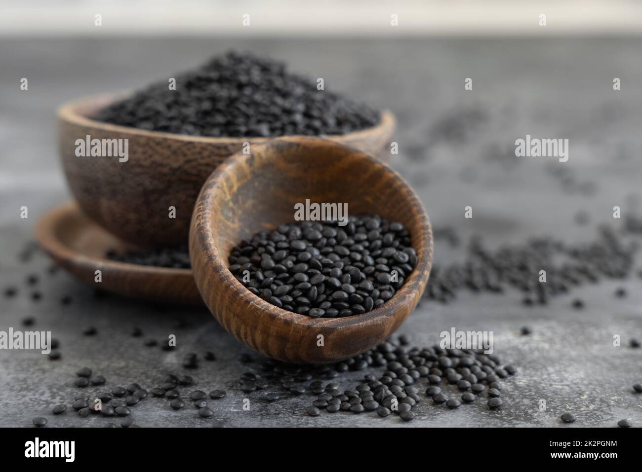 Wooden bowls of dry black lentils beans on grey table close up, protein ...