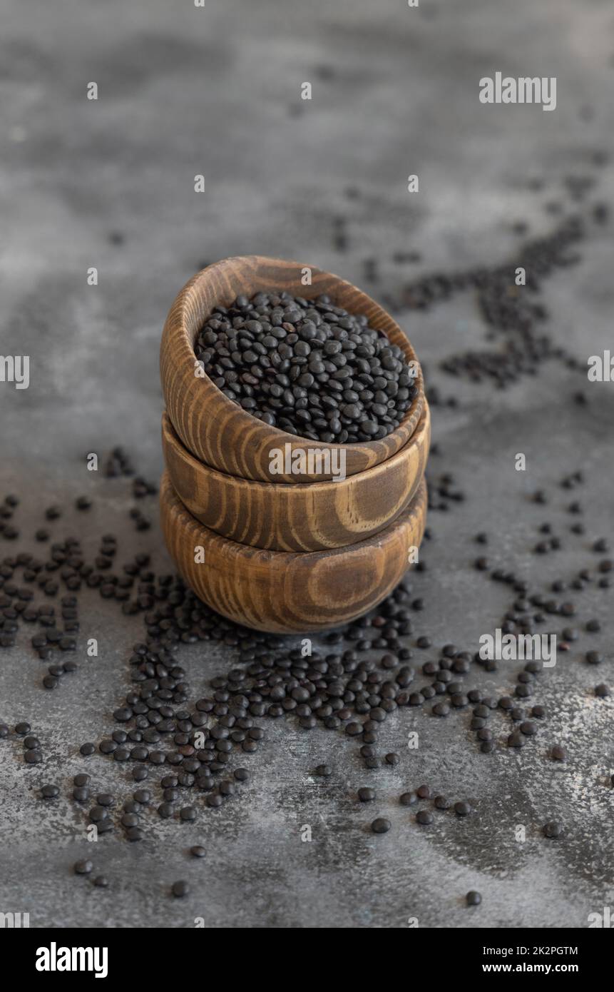 Wooden bowls of dry black lentils beans on grey table close up, protein ...