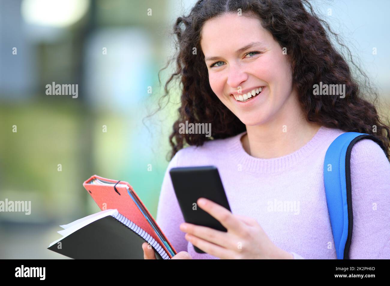 Happy student looking at camera holding phone Stock Photo - Alamy