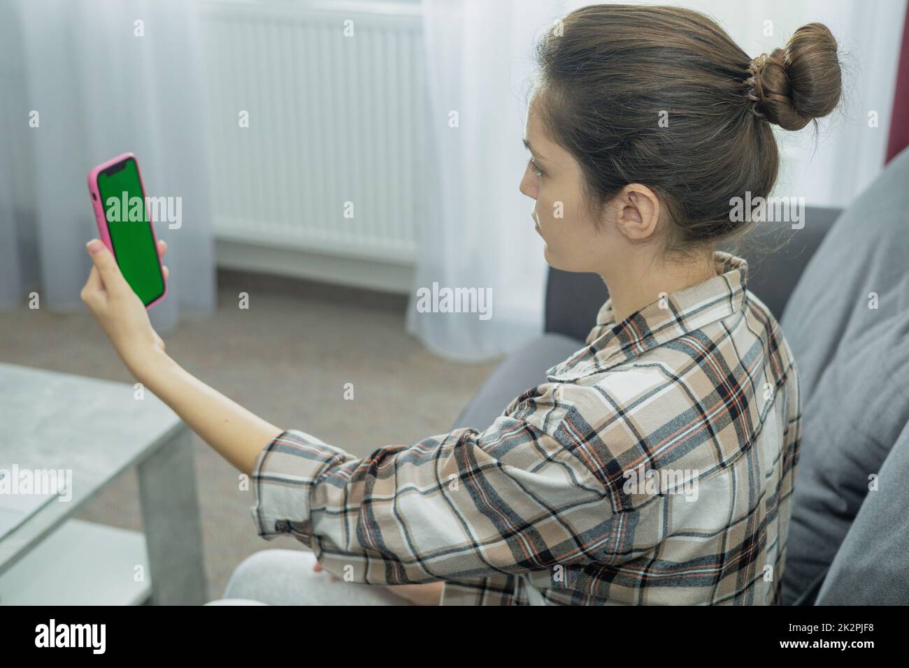 Side view of a girl at a laptop holding a phone in her hands. Modern ...