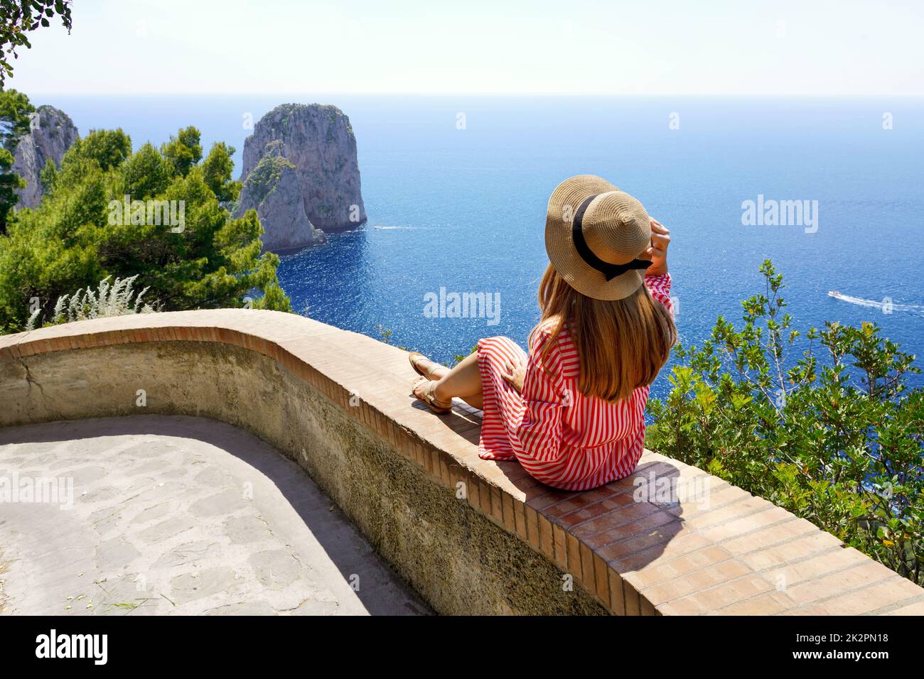 Beautiful young woman with hat sitting on wall looking at stunning ...
