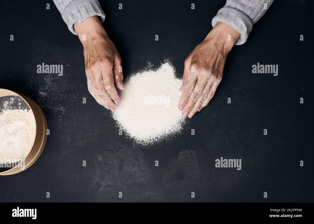 White wheat flour on a black table and two female hands, top view Stock ...