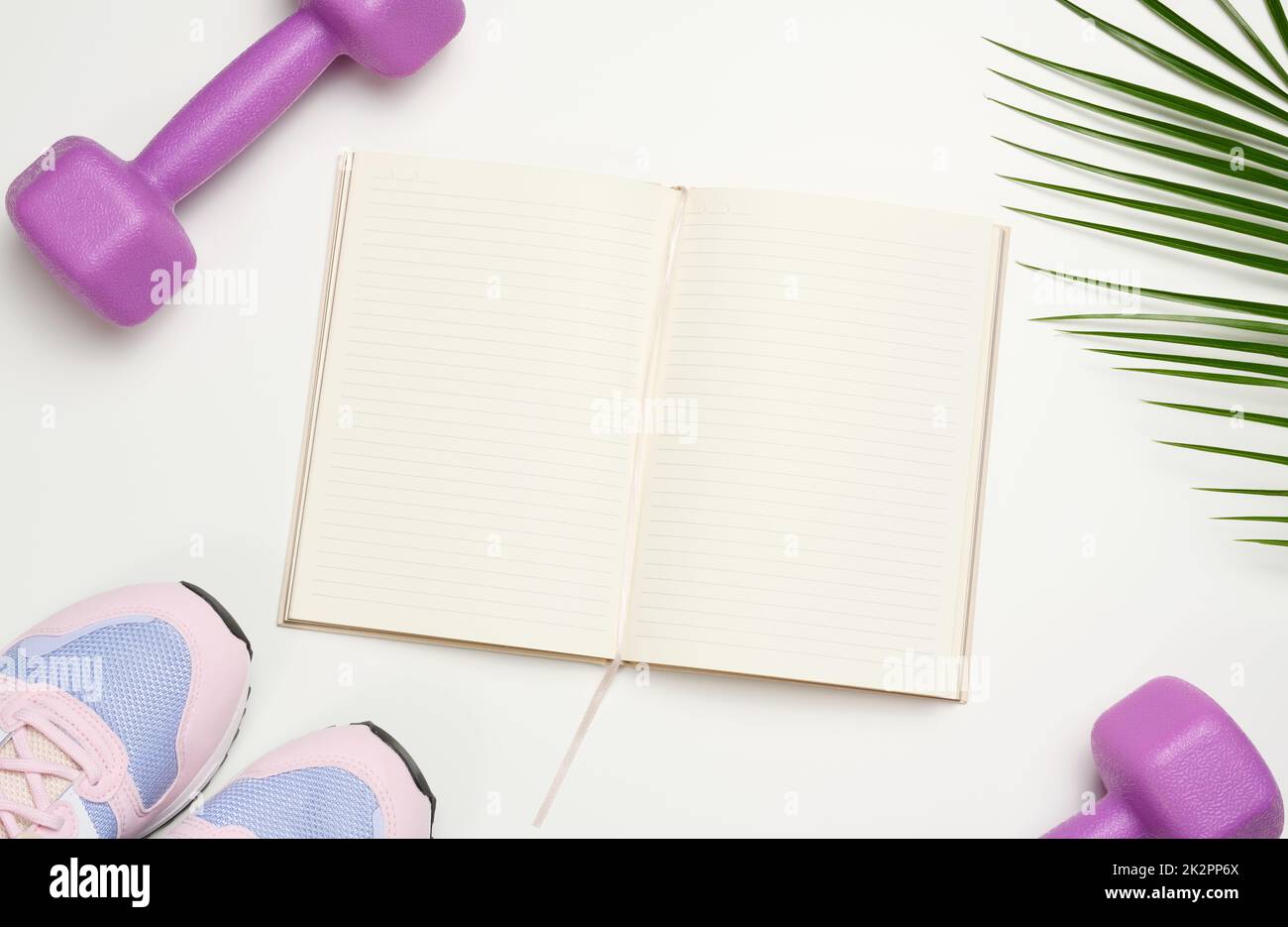 open blank notebook, a pair of sports gym shoes and dumbbells on a ...
