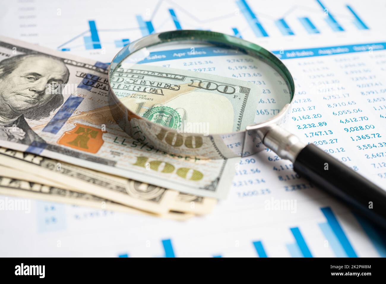 Magnifying glass with US dollar banknotes on charts graphs paper ...