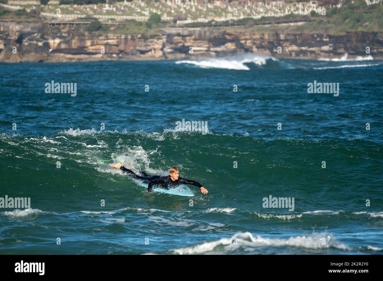 A surfer lying on the shortboard and swimming with hands on the wave ...
