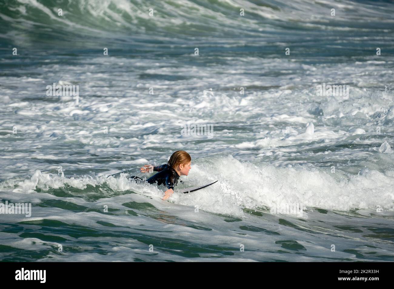 A surfer lying on the shortboard and swimming with hands on the wave ...