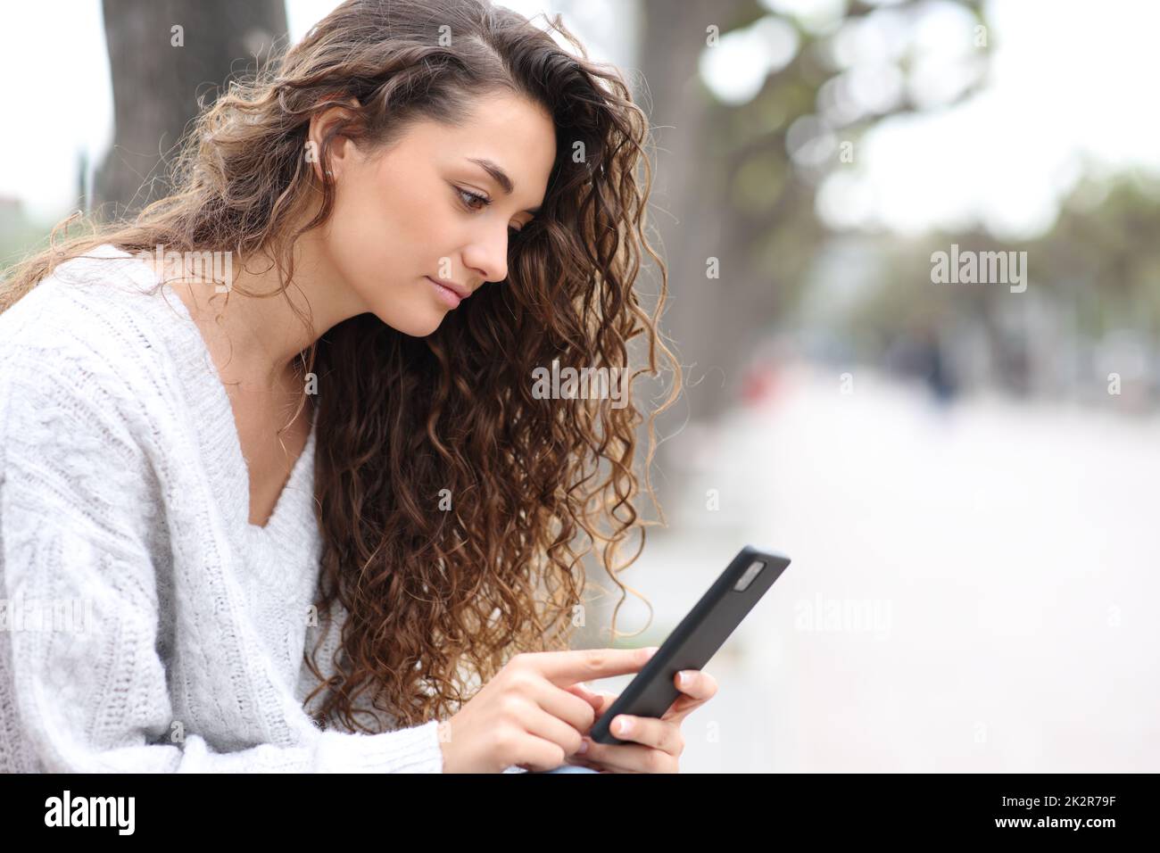 Woman using cell phone sitting on a bench in the street Stock Photo - Alamy
