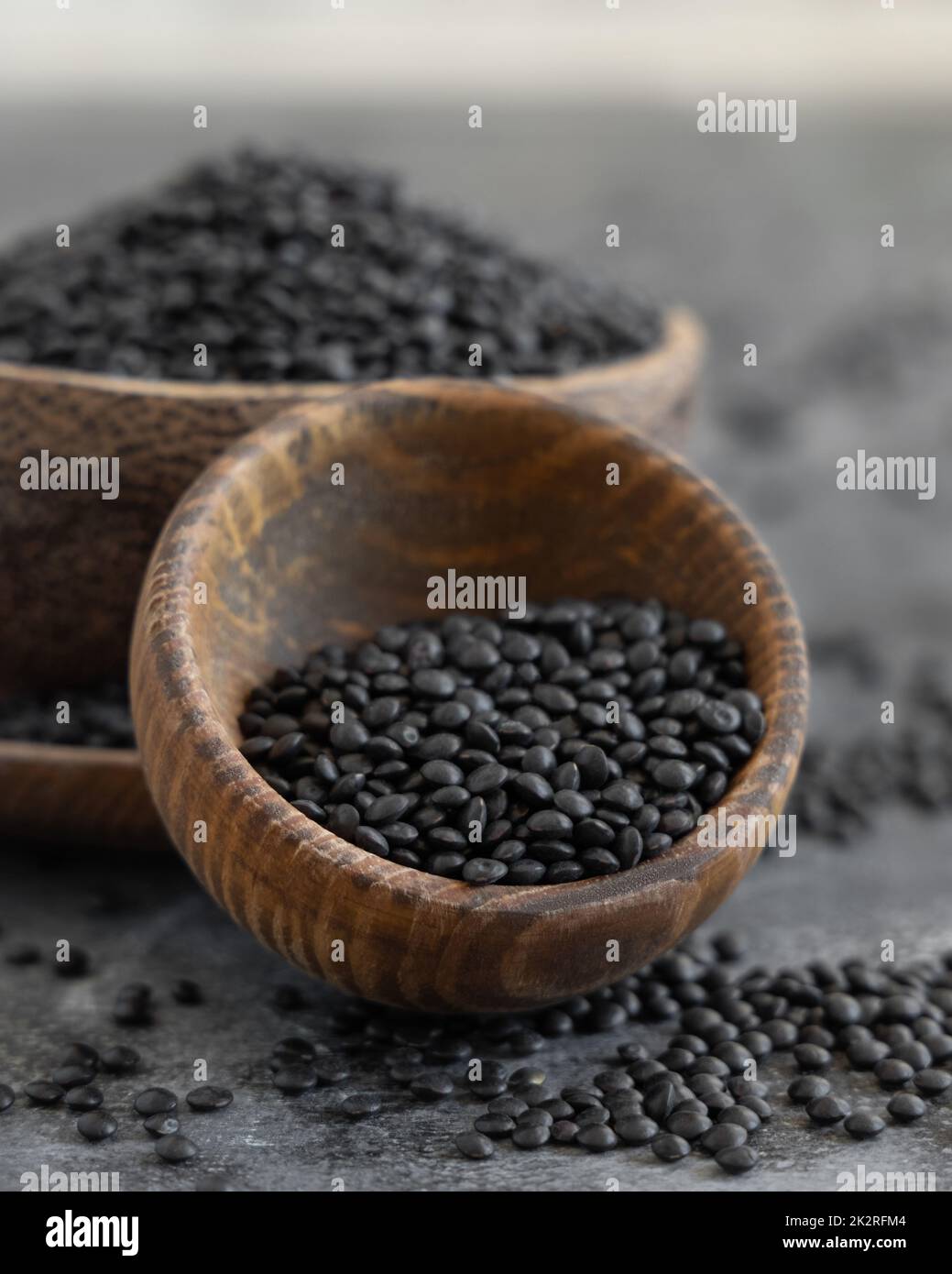 Wooden bowls of dry black lentils beans on grey table close up, protein ...