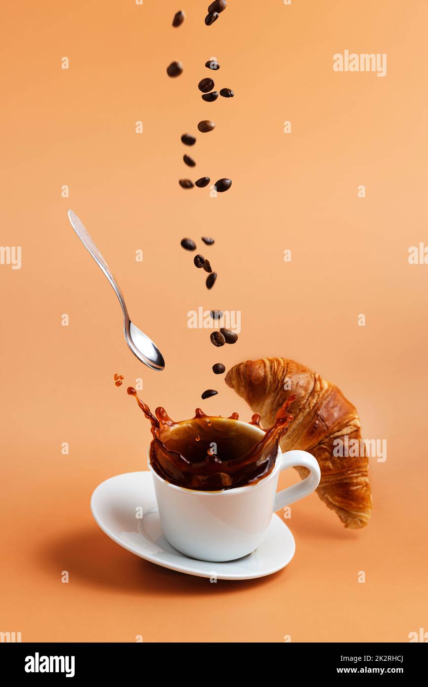 White coffee cup falling on beige table background, splashes, beans ...