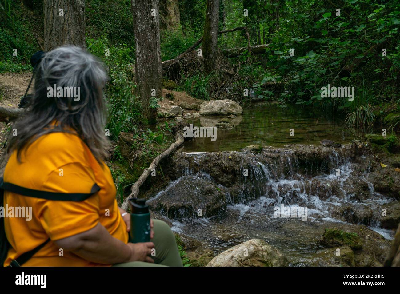 white-haired woman drinking water in a field with a waterfall in the ...