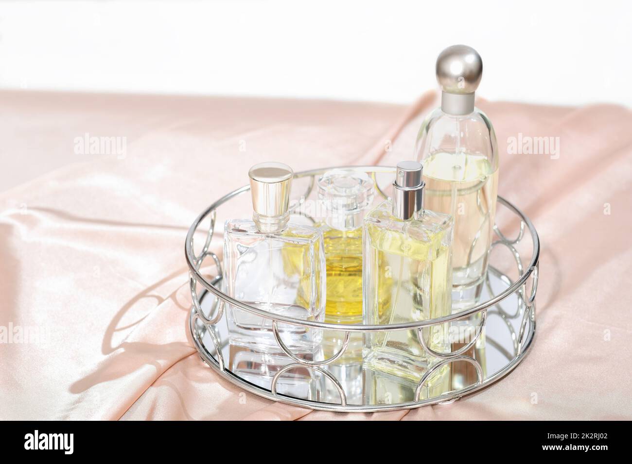 various bottles of perfume on a trendy mirror tray. pink silk satin ...