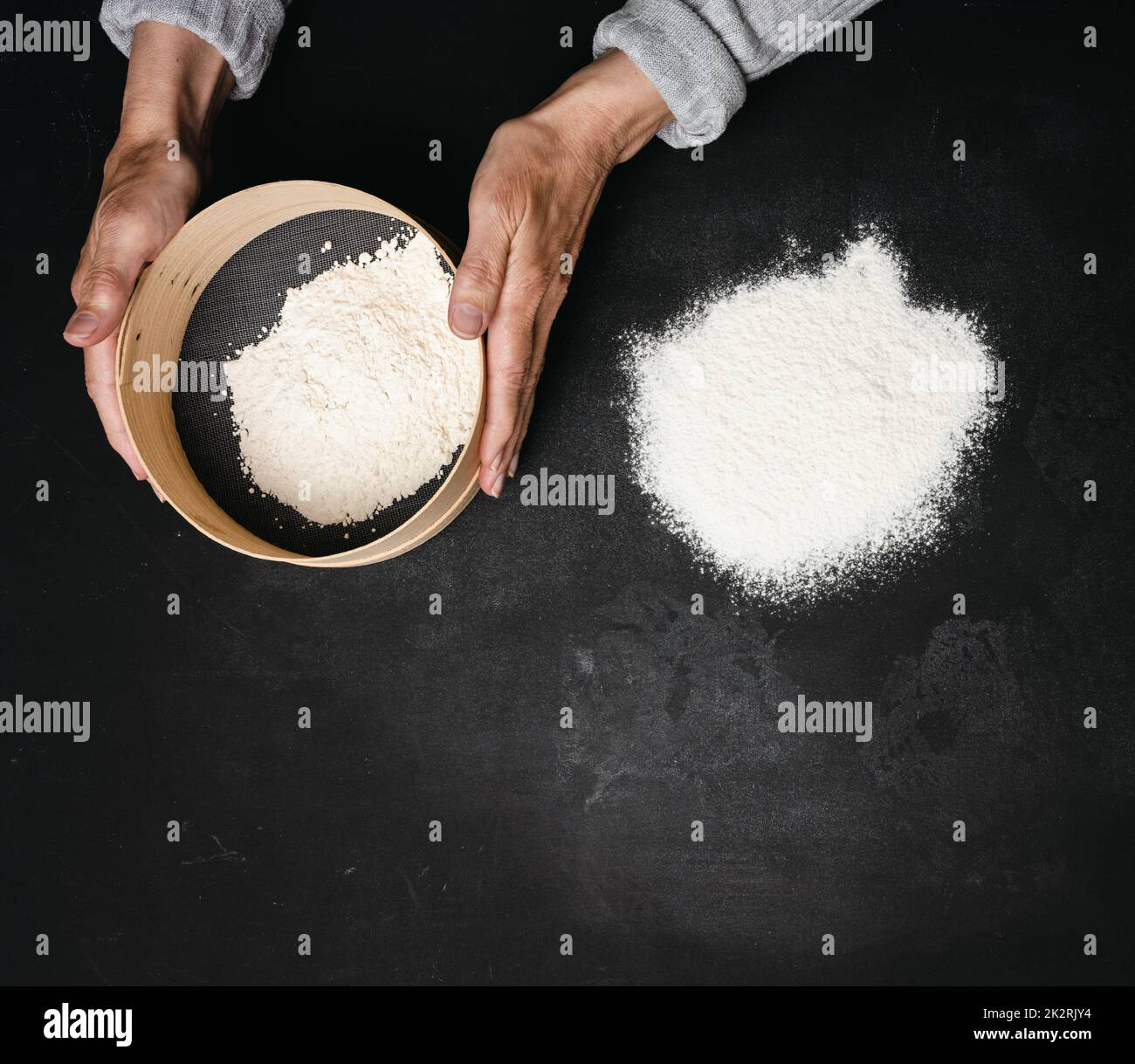 two female hands hold a round wooden sieve with wheat flour on a black ...