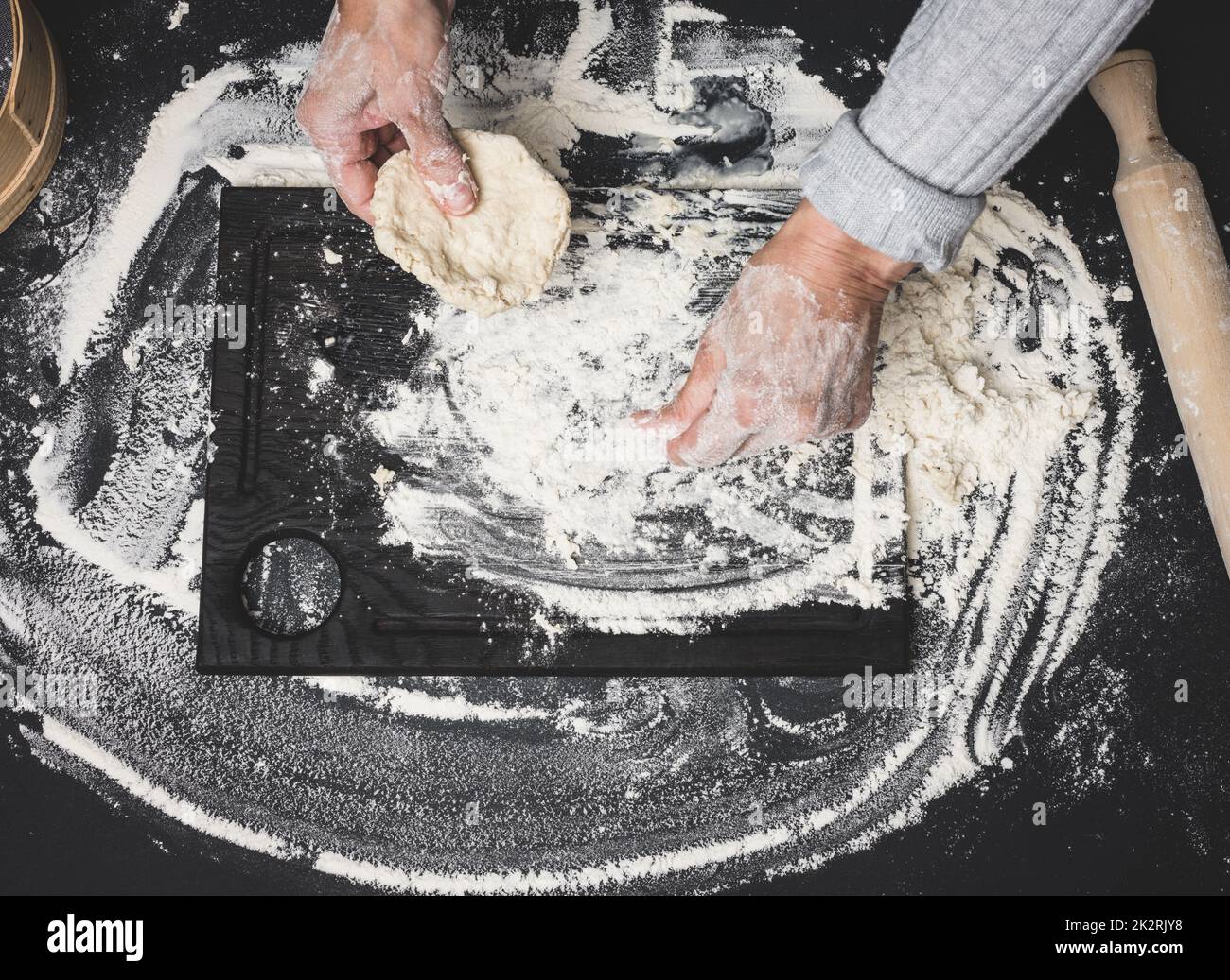 two female hands knead the dough from white wheat flour on a black ...