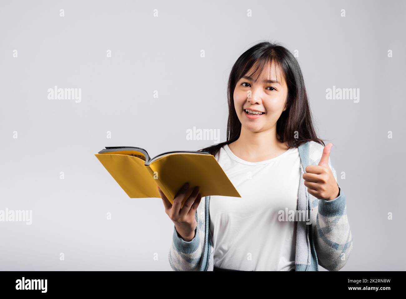 Woman teen smiling holding open book and show thumb up finger for good ...