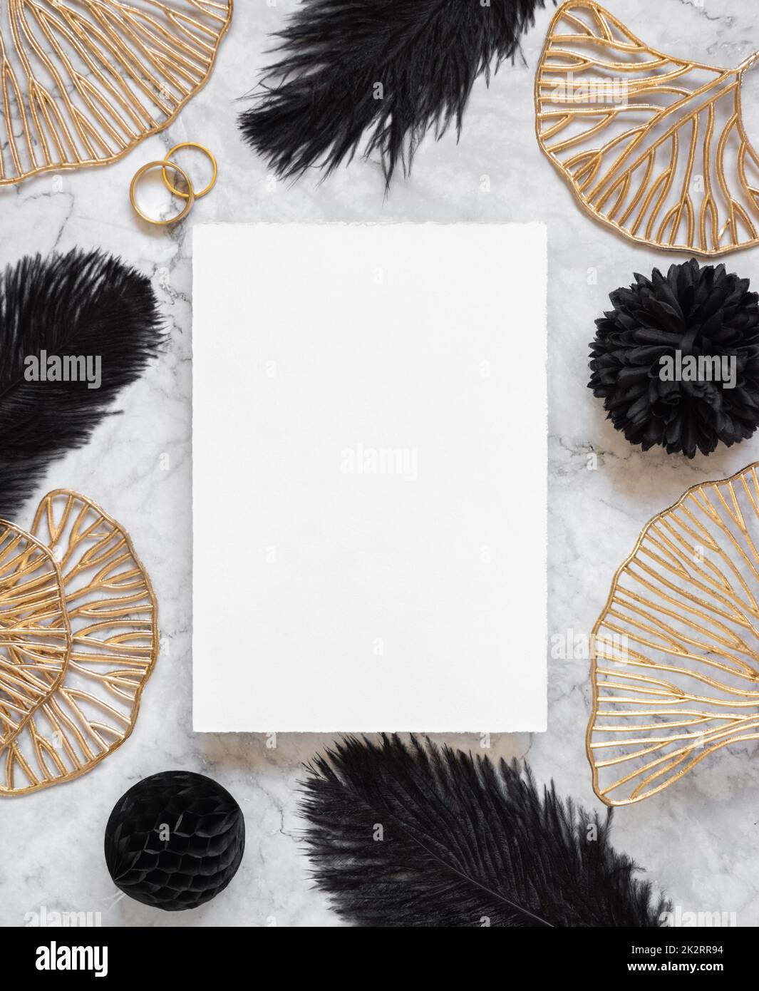Blank card on marble table near black feathers and golden leaves with ...