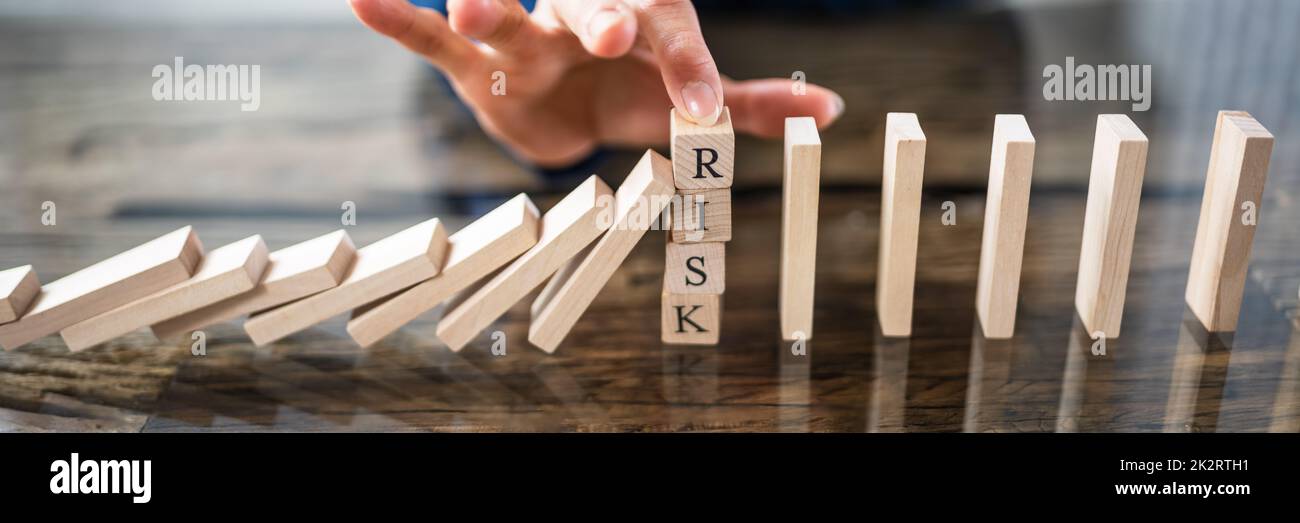 Businessperson's Finger Stopping Domino From Falling Stock Photo - Alamy