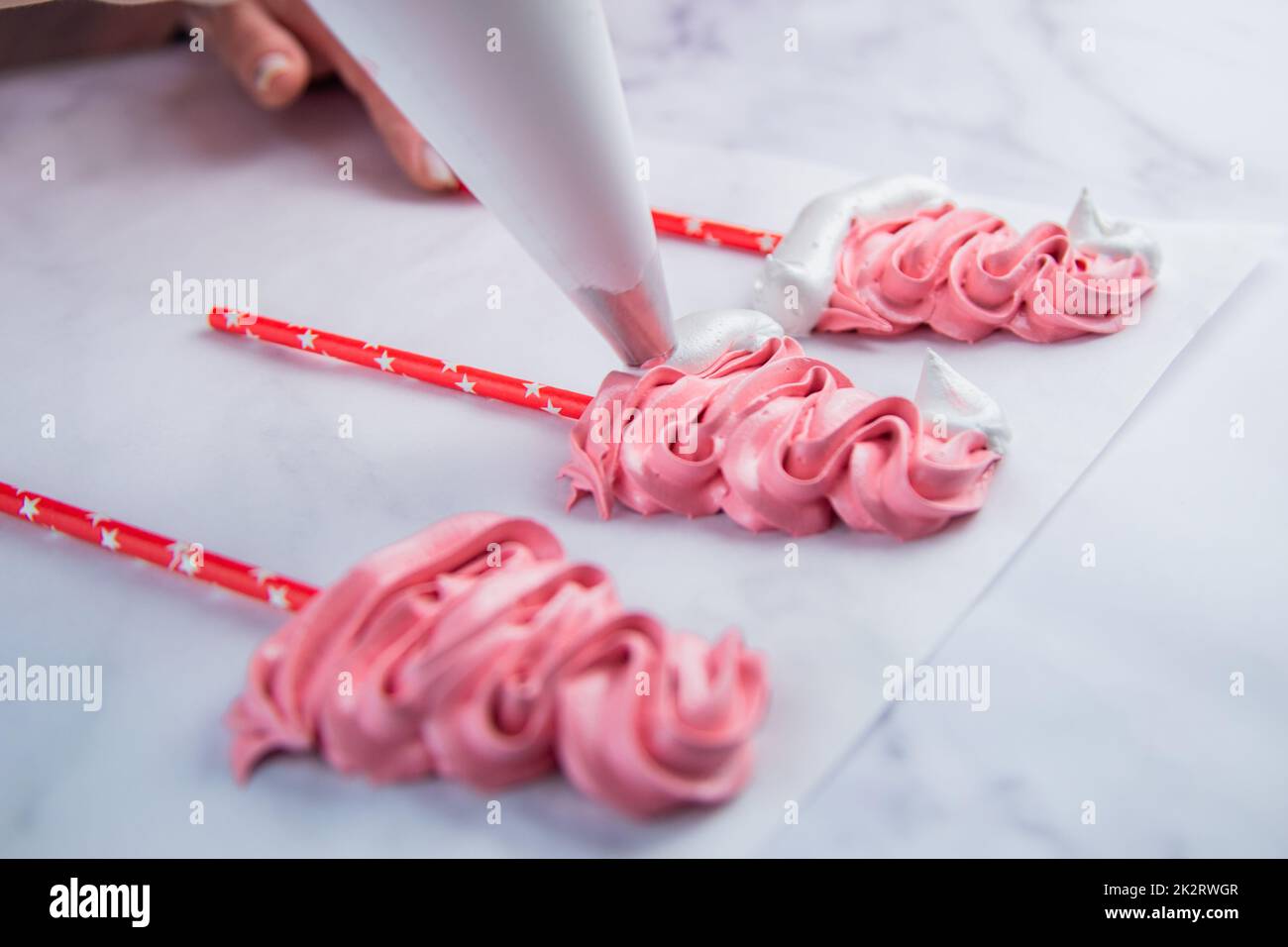 On light parchment there are pink meringue caps on sticks, the cook ...