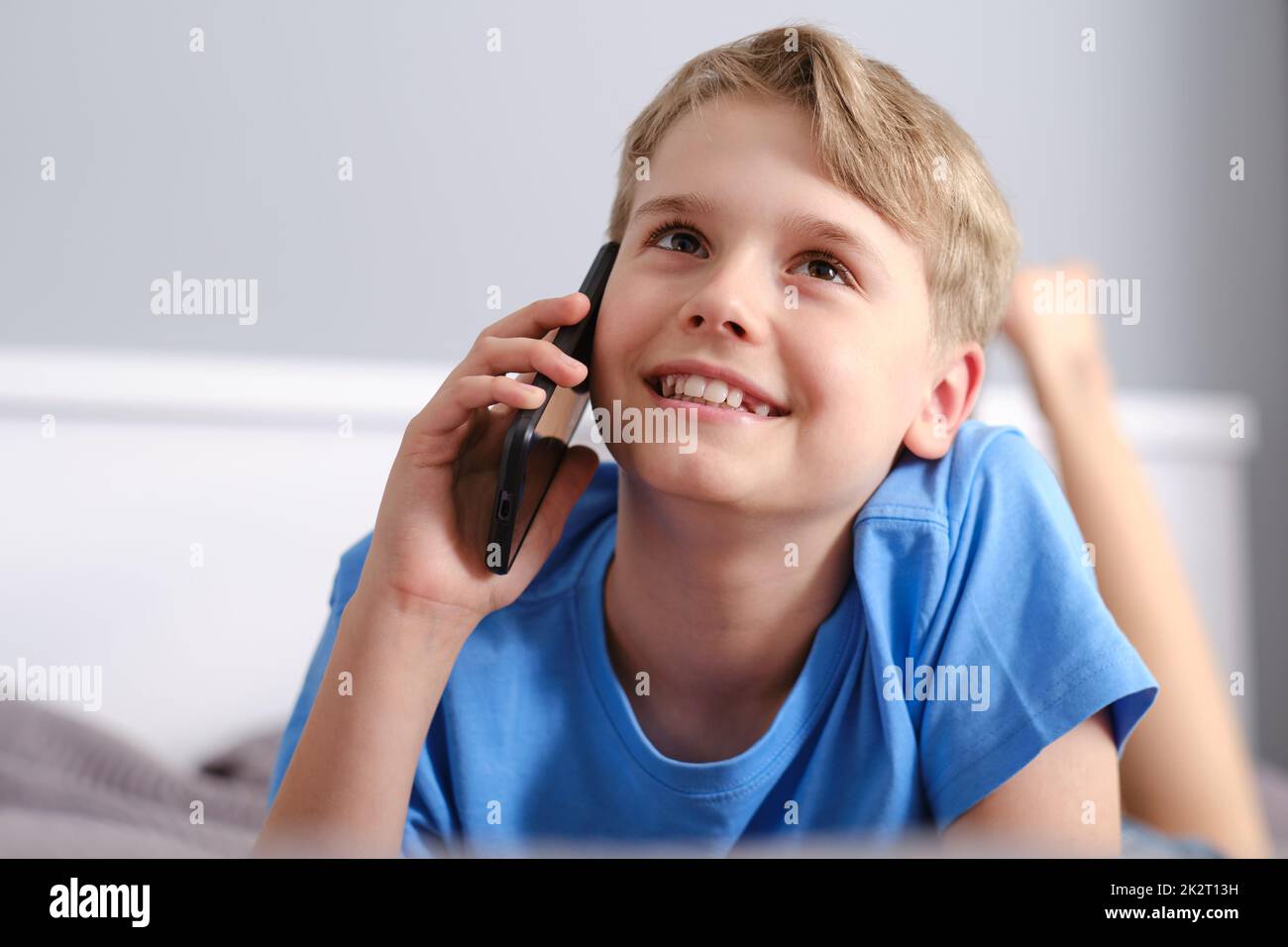 Closeup portrait of a cute boy talking on the phone while lying on the ...