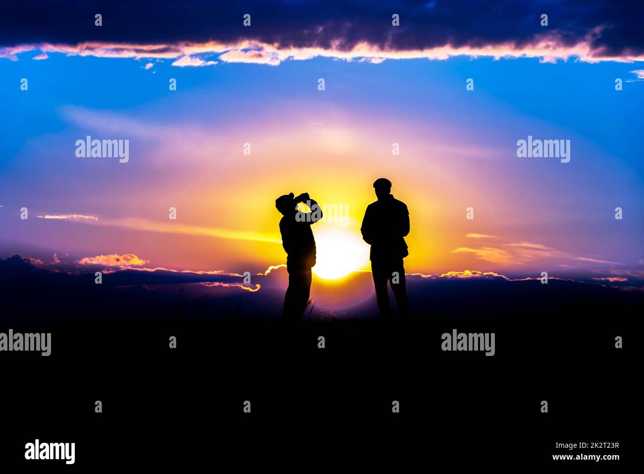 Two silhouettes of men talking and drinking a drink a jar at sunset or ...