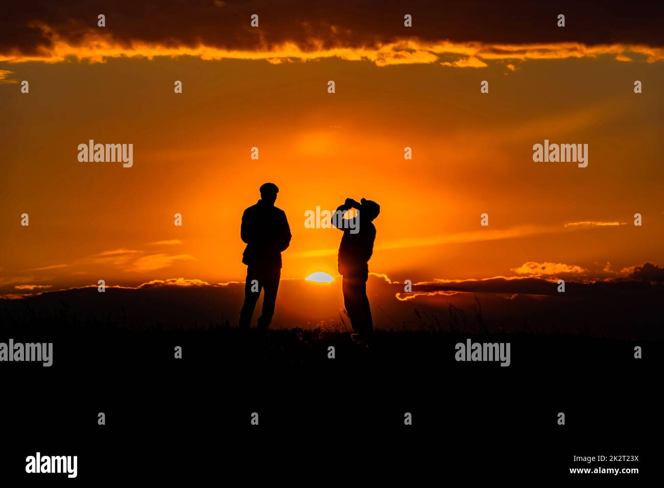 Two silhouettes of men talking and drinking a drink a jar at sunset or ...
