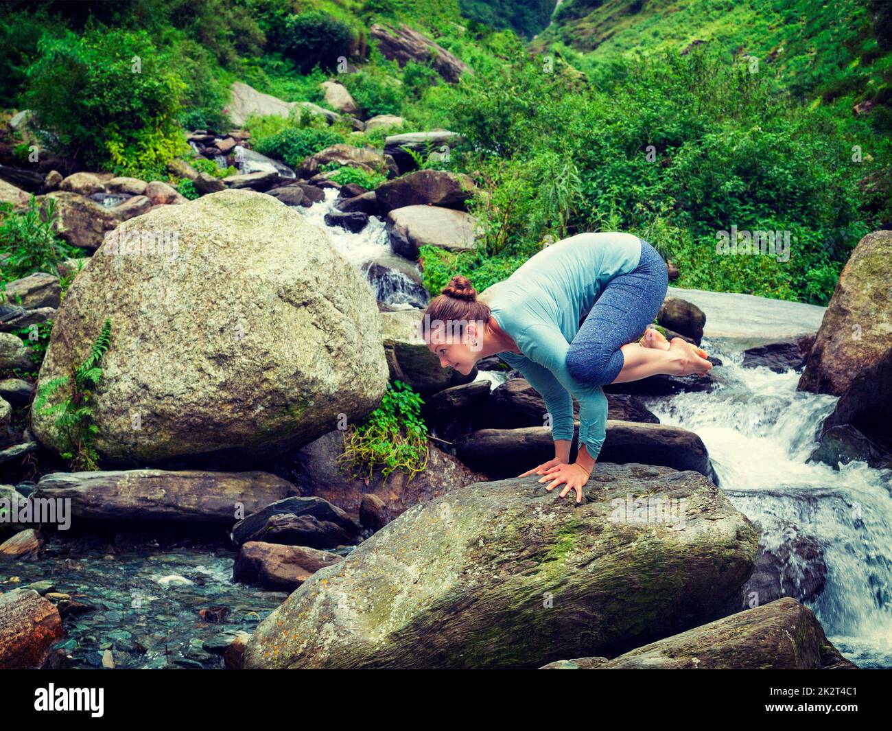 Woman doing Kakasana asana arm balance at waterfall Stock Photo - Alamy