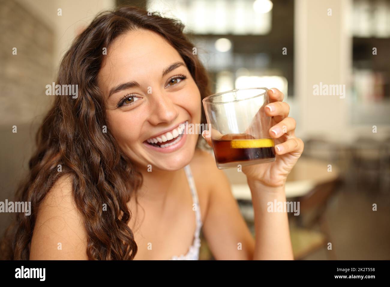 Happy woman in a bar holding refreshment glass looks at you Stock Photo ...