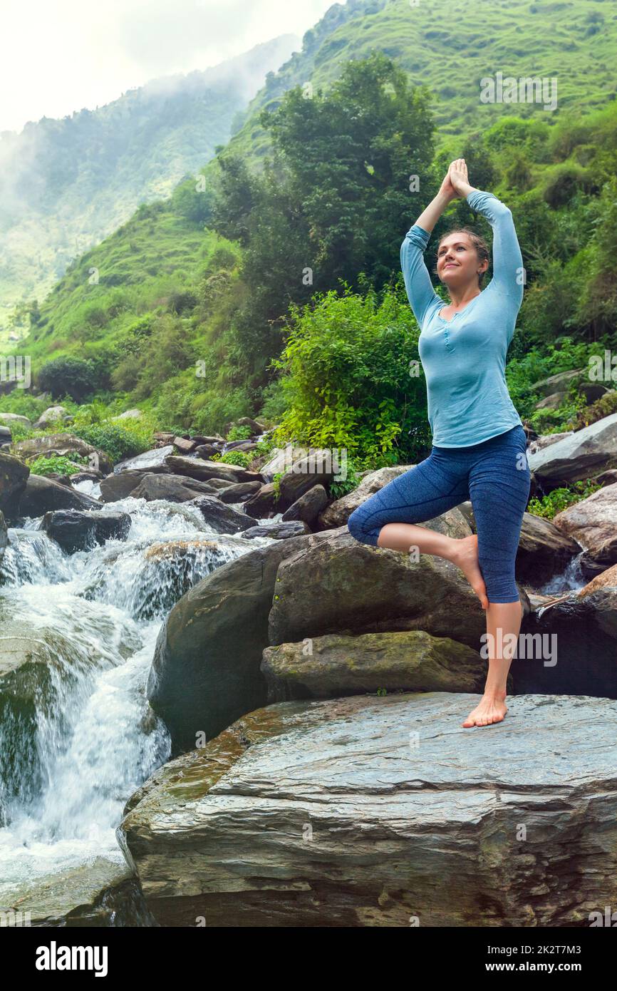Woman in yoga asana Vrikshasana tree pose at waterfall outdoors Stock ...