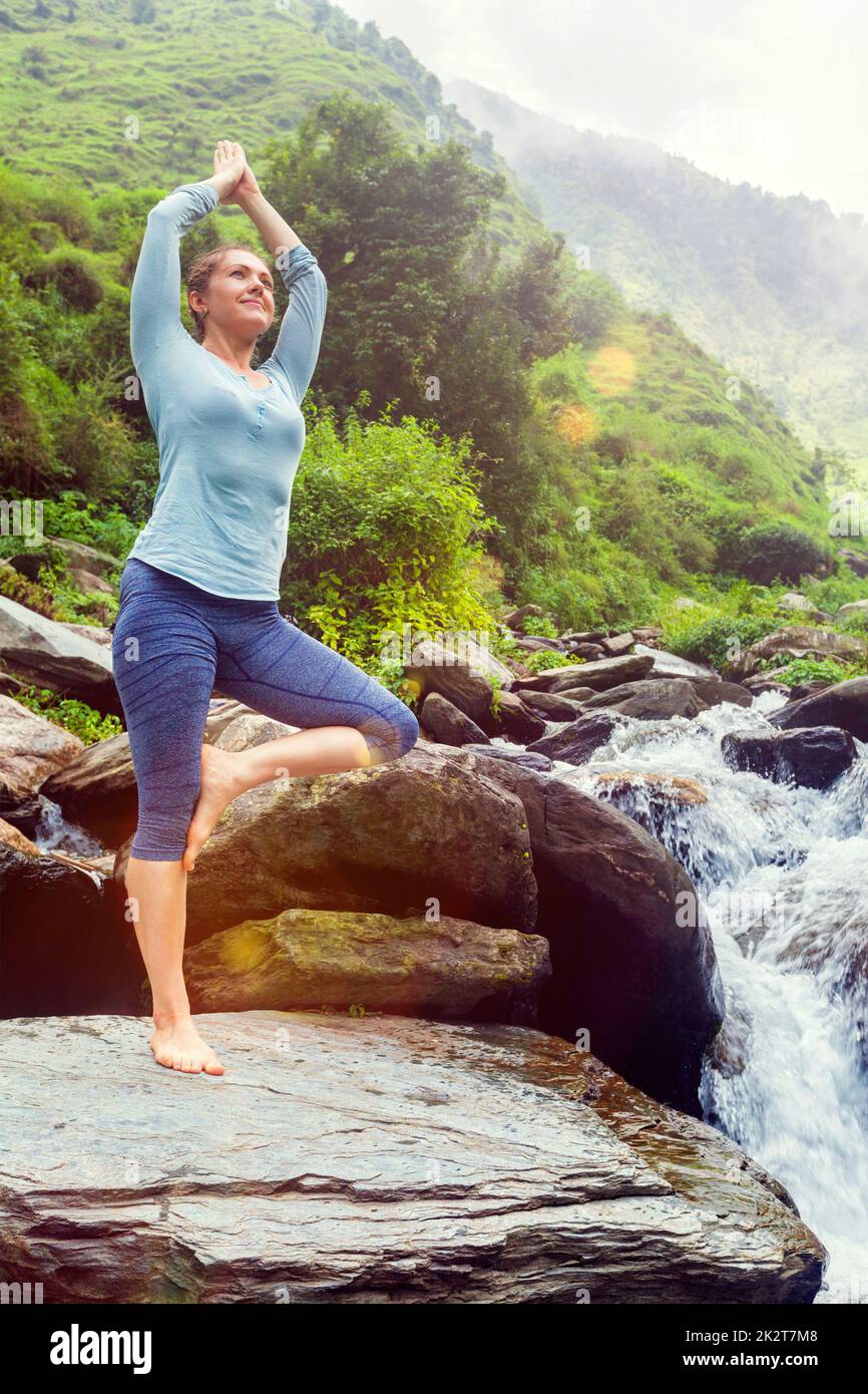 Woman in yoga asana Vrikshasana tree pose at waterfall outdoors Stock ...