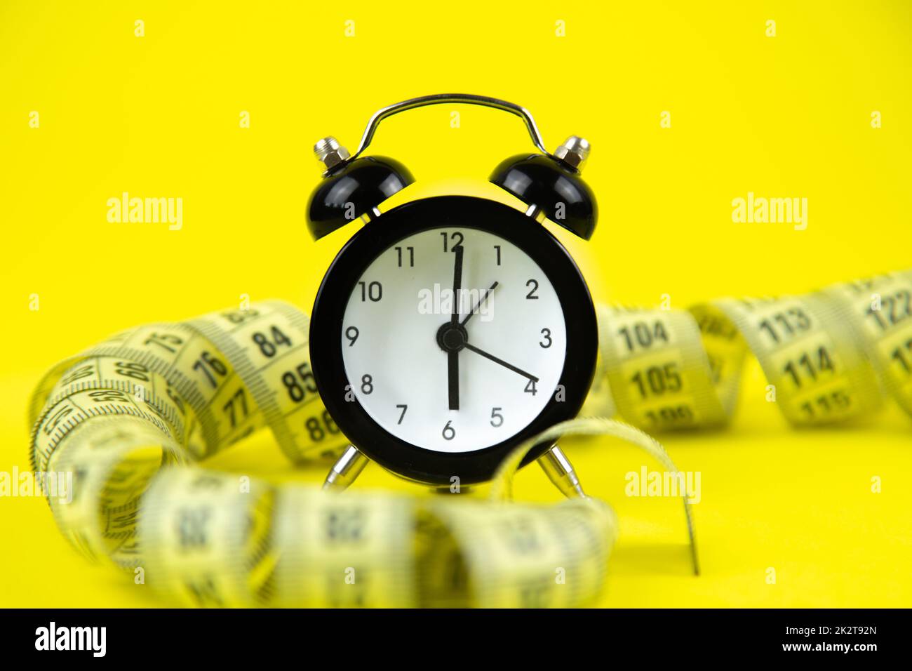 A black alarm clock with a white dial stands on a bright yellow ...