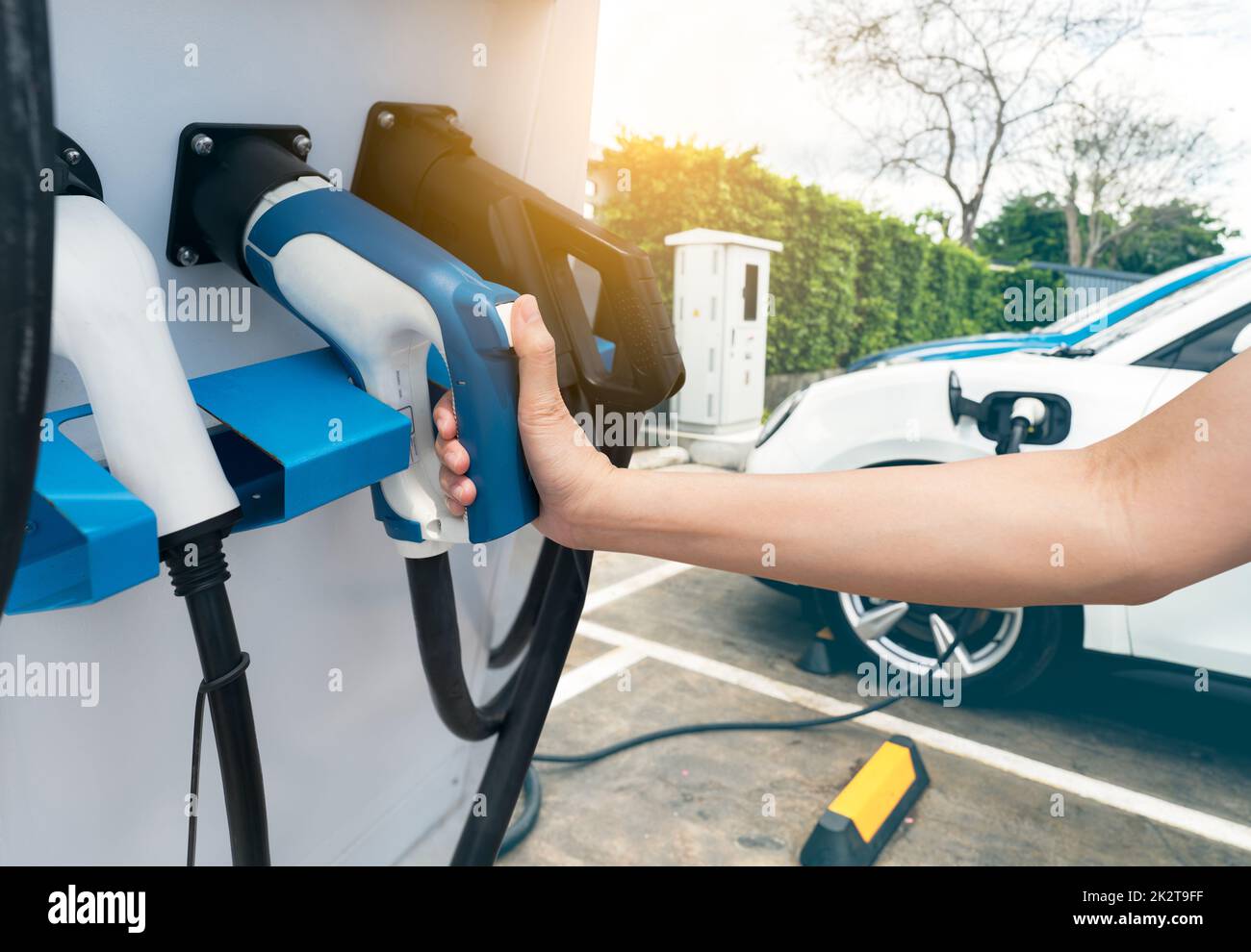 Hand holding electric plug-in charger on blur car charging. EV car ...