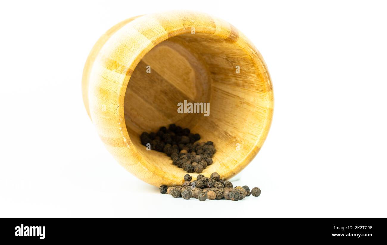 Black pepper pouring from the wooden bowl isolated on white background ...