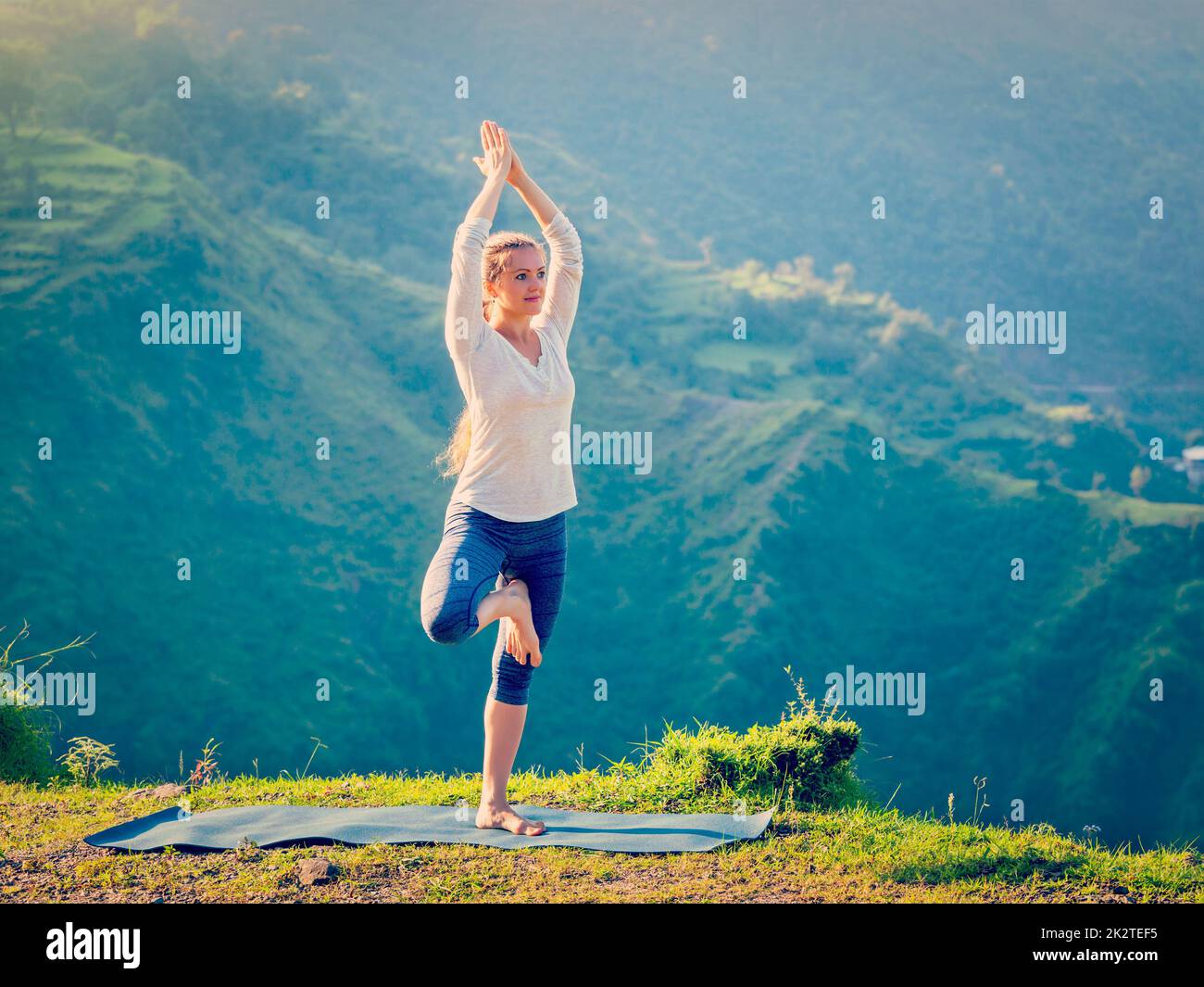 Woman doing yoga asana Vrikshasana tree pose in mountains outdoors ...