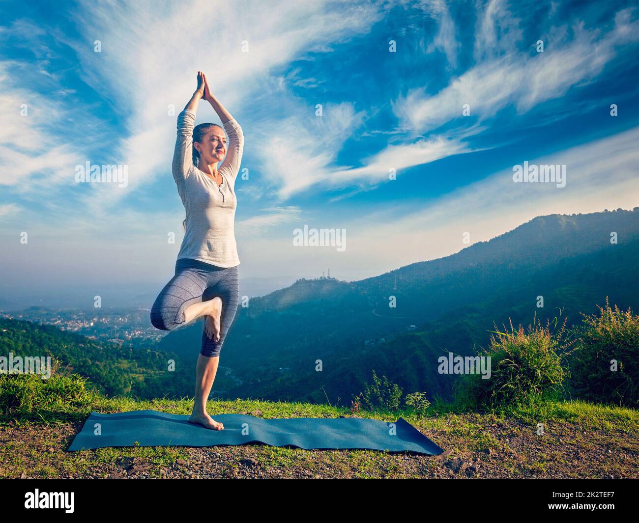 Woman doing yoga asana Vrikshasana tree pose in mountains outdoors ...