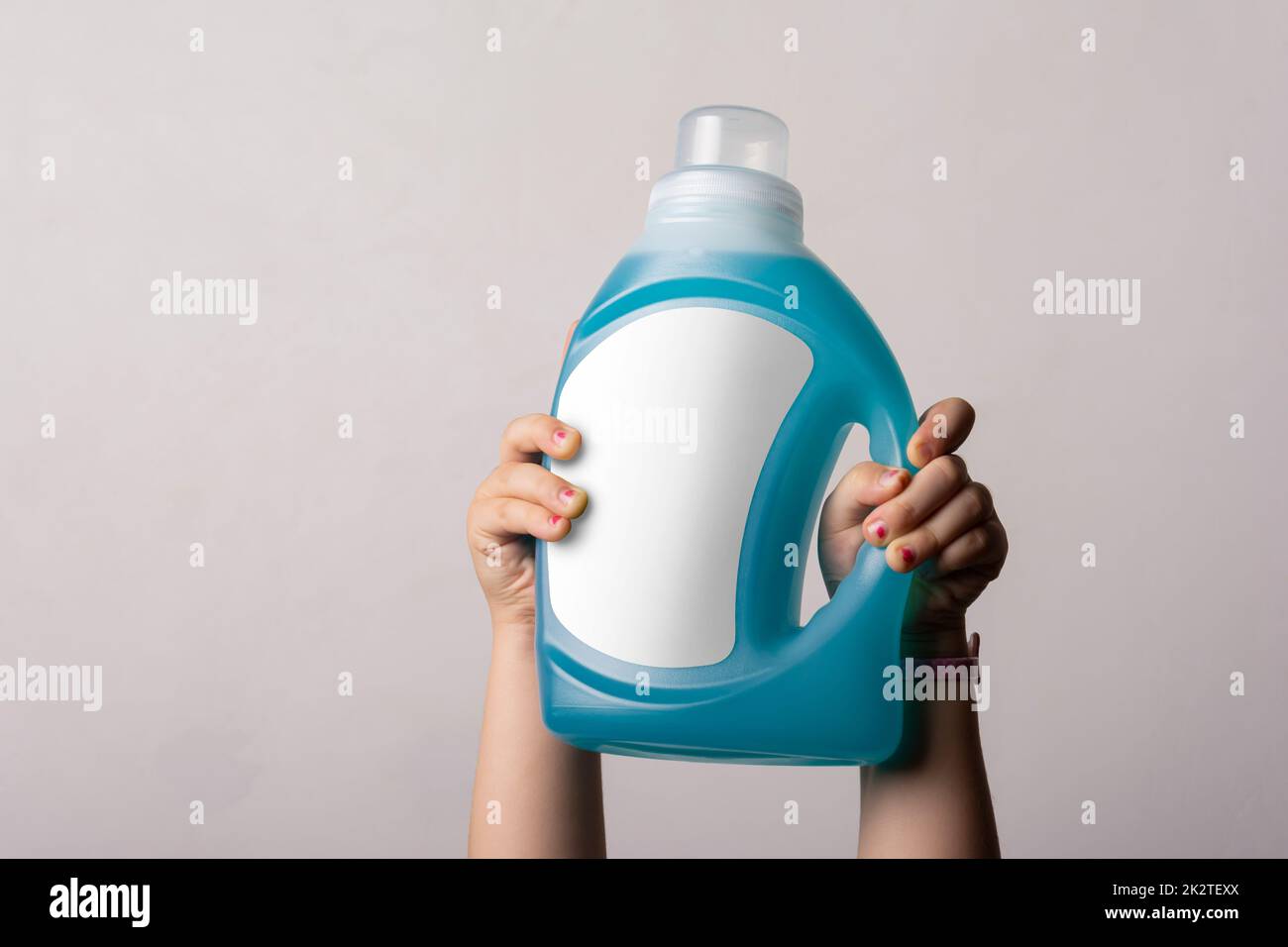 Cloth detergent liquid bottle at little girl hands in front of light ...