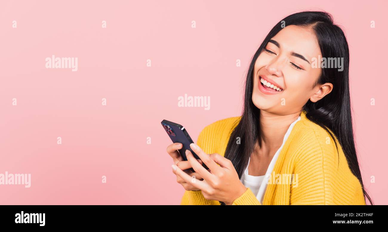 Happy Asian portrait beautiful cute young woman excited laughing holding mobile phone, studio ...