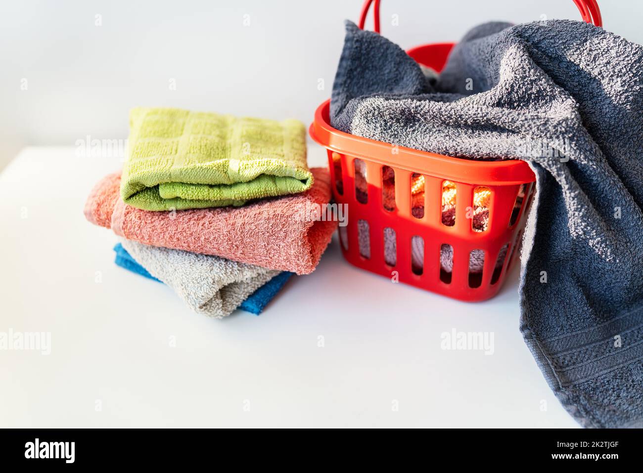 Multi-colored towels lie in a red laundry basket on a white background ...