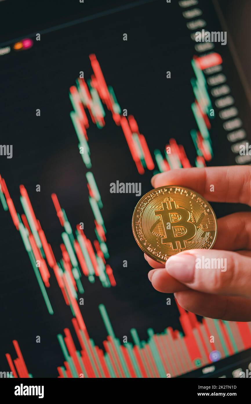 Hand holding a gold Bitcoin coin with candle stick graph chart and ...