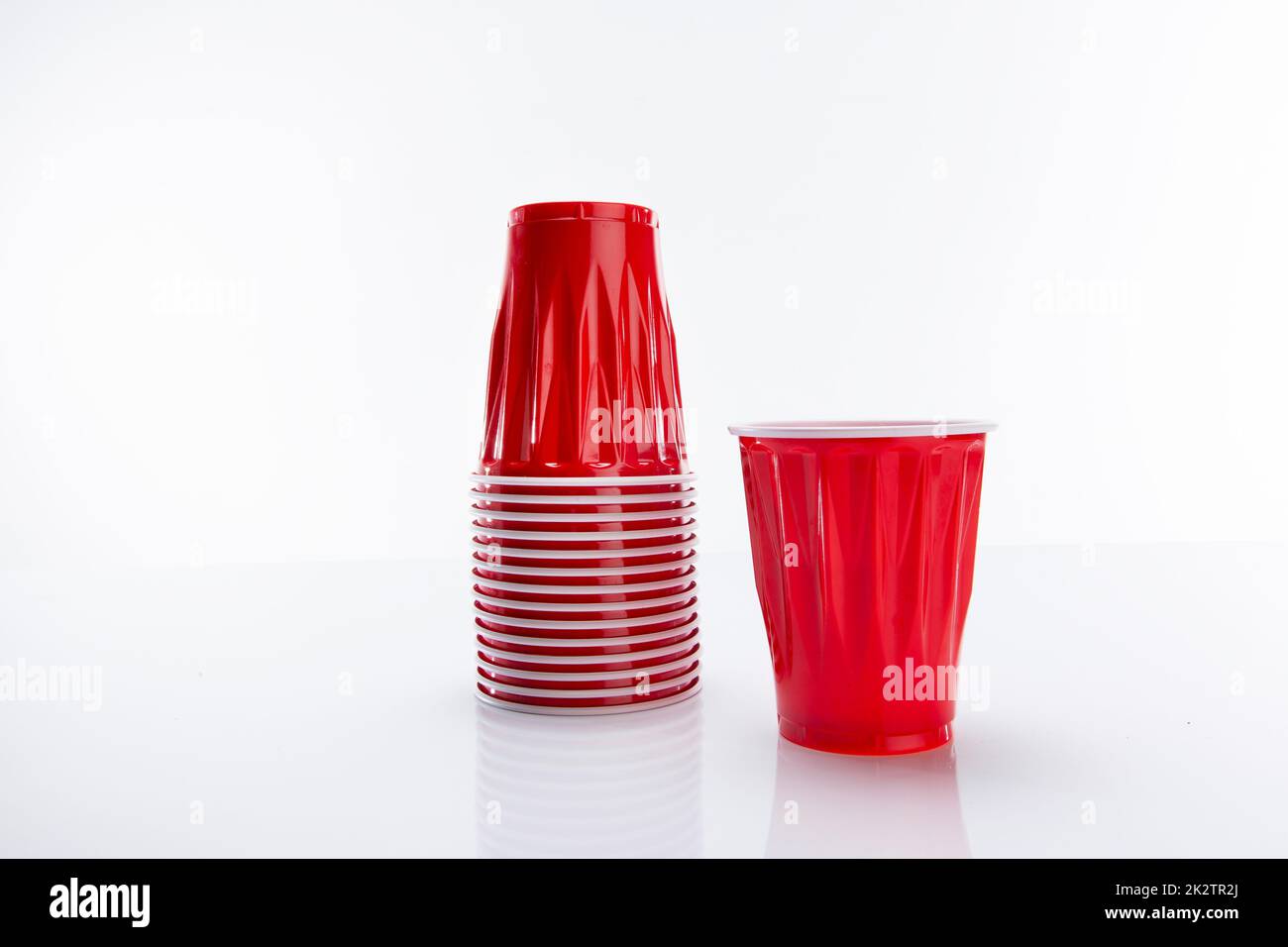 A red disposable plastic cup put next to a horizontal stack of cups ...