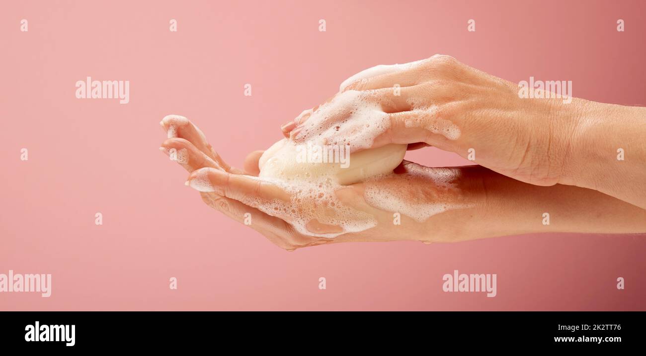 Young woman cleaning hands with foamy soap on a bright pink background ...