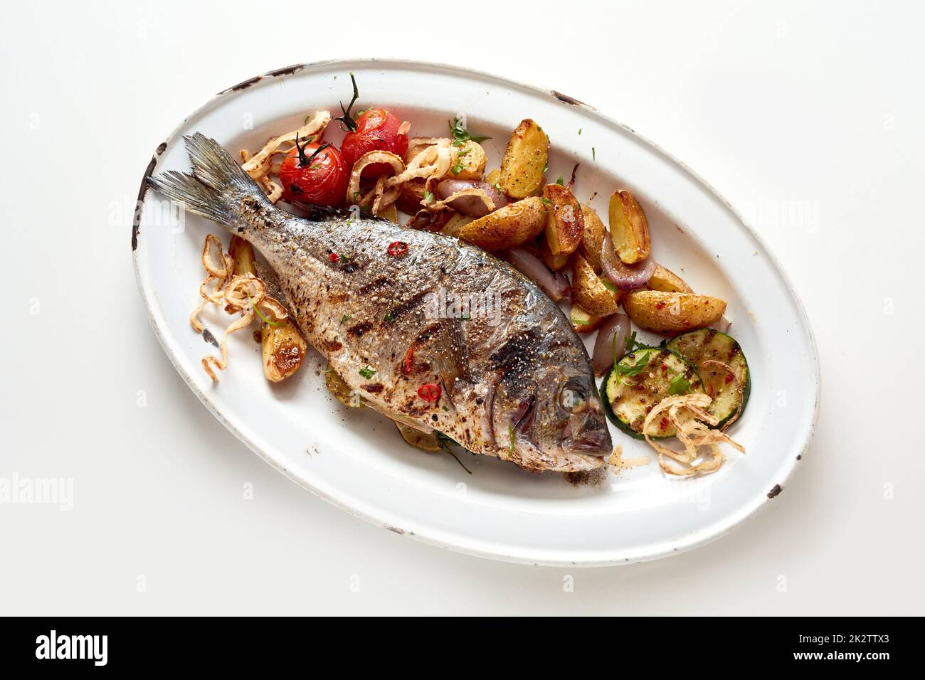Appetizing roasted fish served with vegetables and potatoes against ...