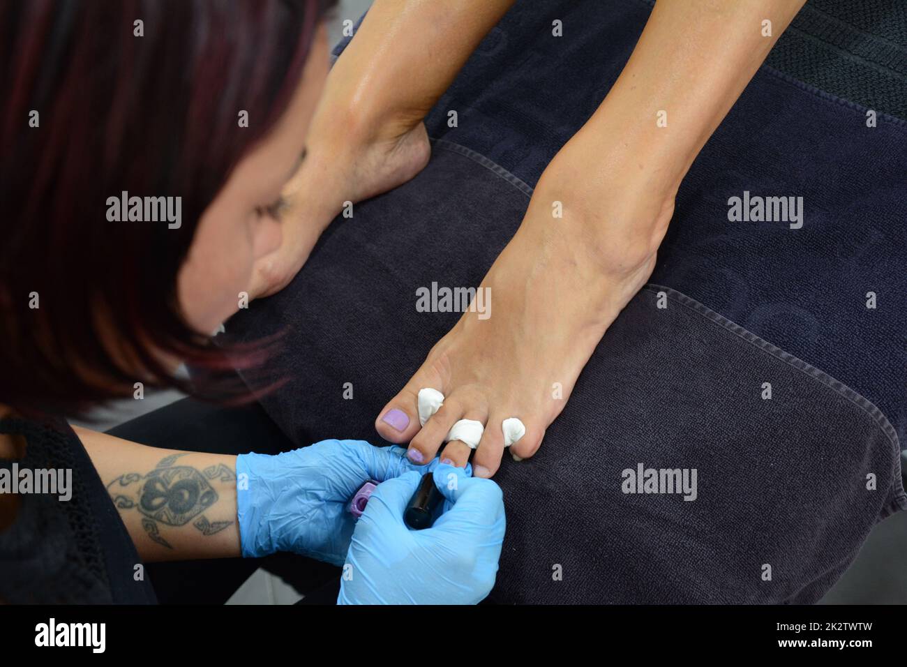 A nail master with black gloves applying a light purple pedicure on a ...