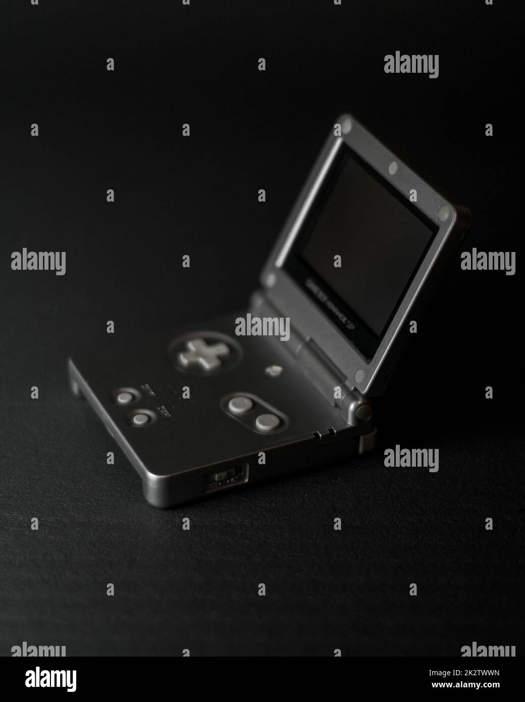 A vertical shot of a vintage gray Game Boy Advance SP on a dark surface ...