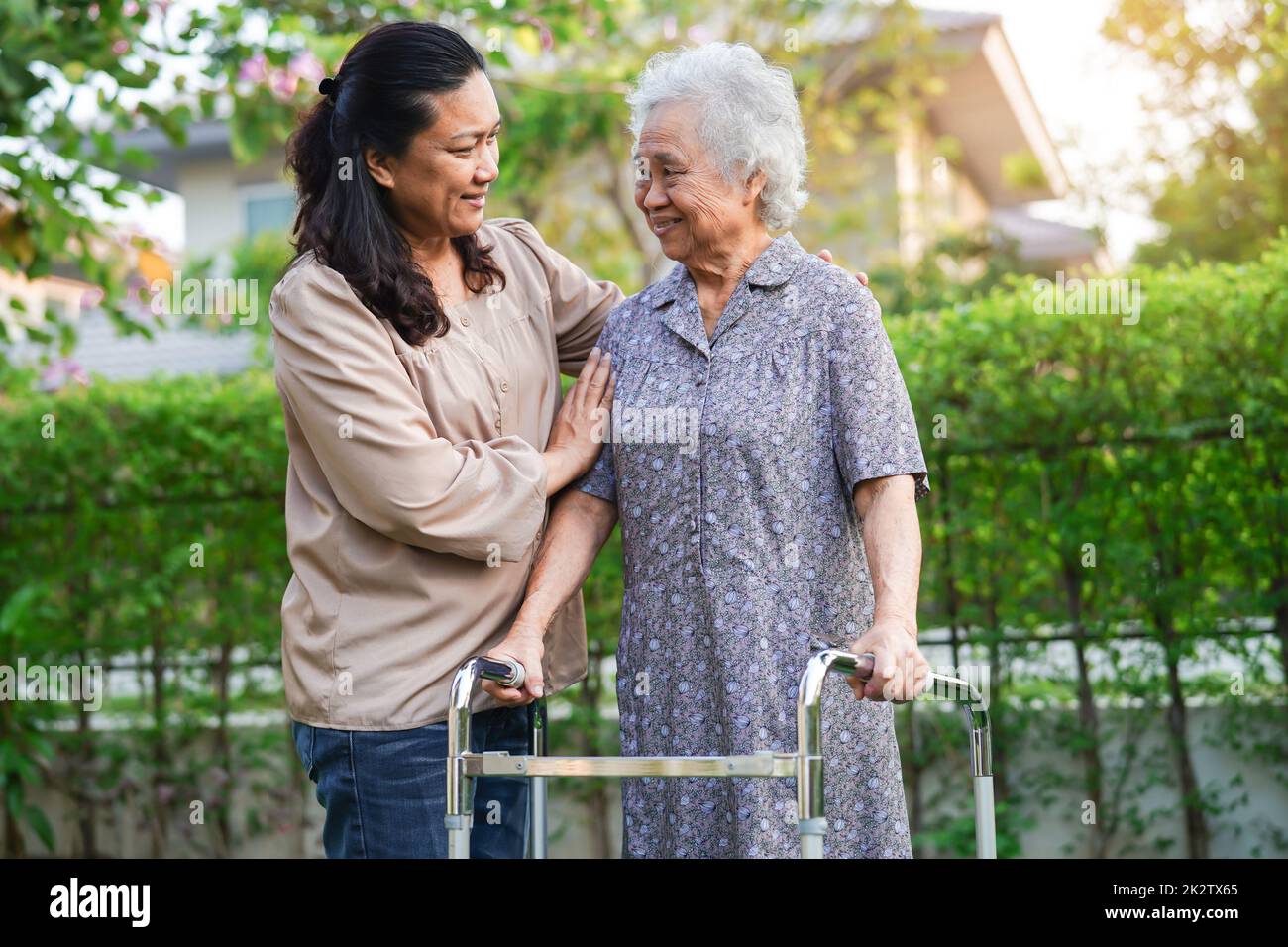 Caregiver help Asian elderly woman disability patient walk with walker in park, medical concept ...