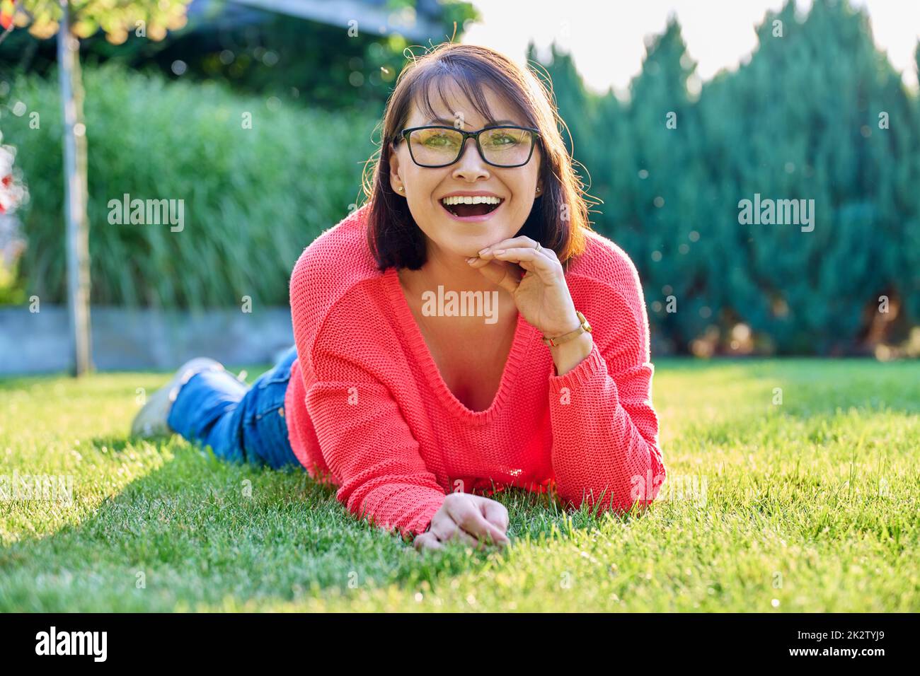 Outdoor Portrait Of Smiling Middle Aged Woman Lying On Grass Stock