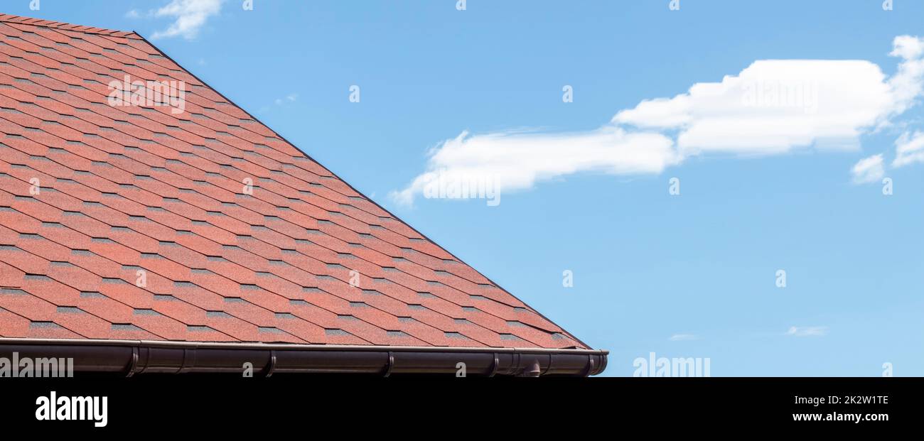 New roof with red shingles against the blue sky. Tiles on the roof of ...