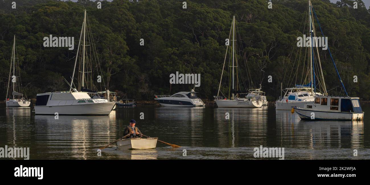 The man rowing a boat at sunrise with the white yachts floating on ...